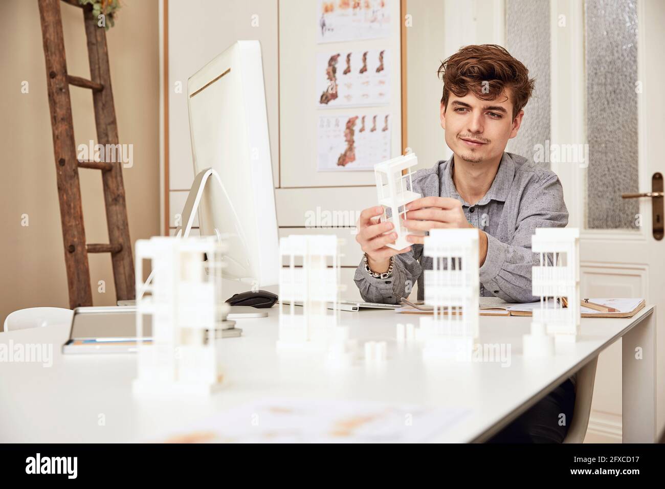 Male architect examining architectural model while sitting at table ...