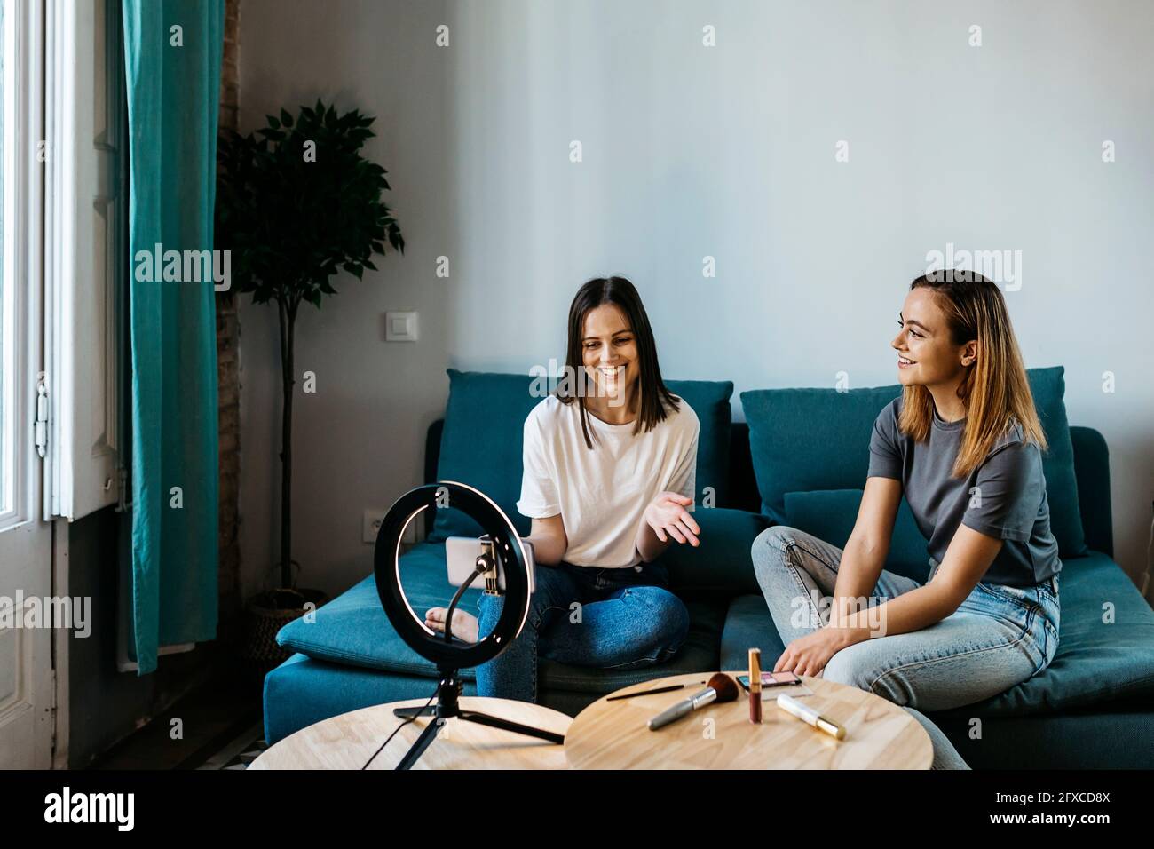 Smiling influencer gesturing while vlogging with girlfriend at home ...