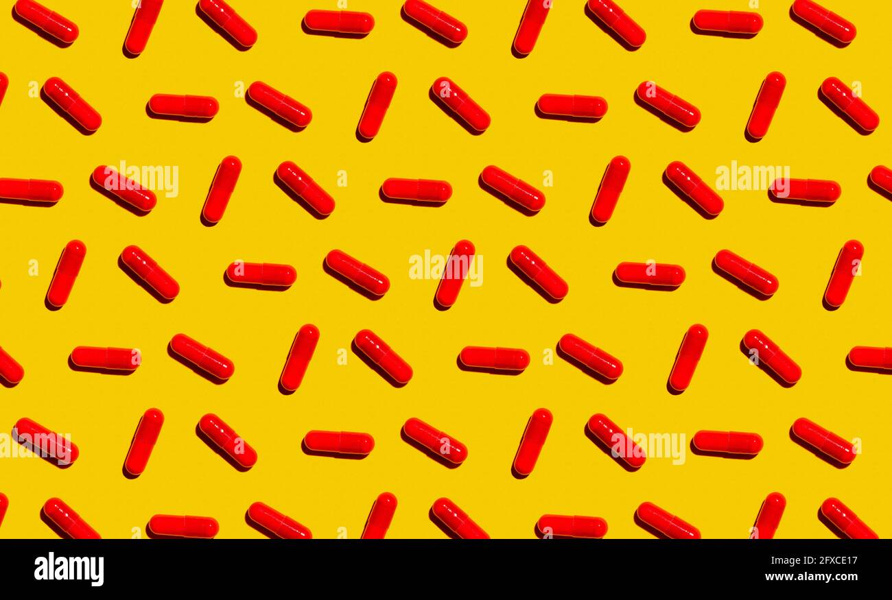 Pattern of rows of red medicine capsules laid against yellow background ...