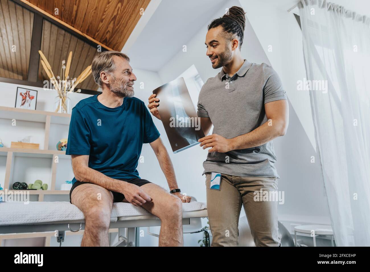 Male physical therapist discussing x-ray image of knee with patient at ...