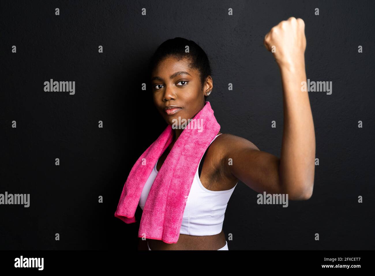 Smiling woman flexing muscles while standing in front of black ...