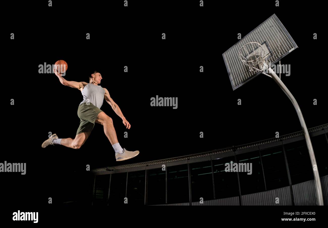 Young man jumping while playing basketball at night Stock Photo - Alamy
