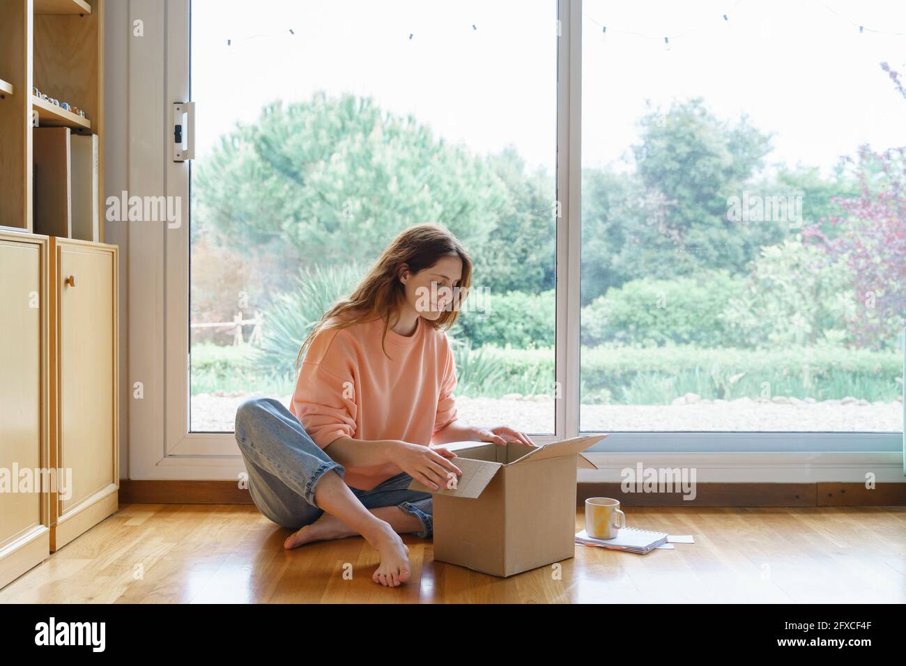 Beautiful woman opening cardboard box while sitting at home Stock Photo ...