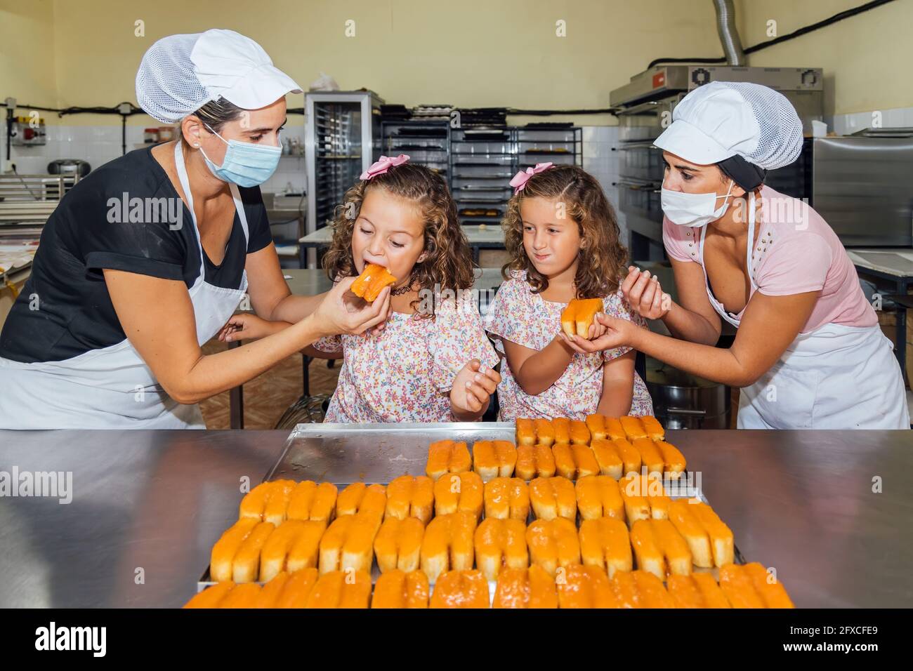 Women wearing protective face mask feeding pastry to twin girls in ...