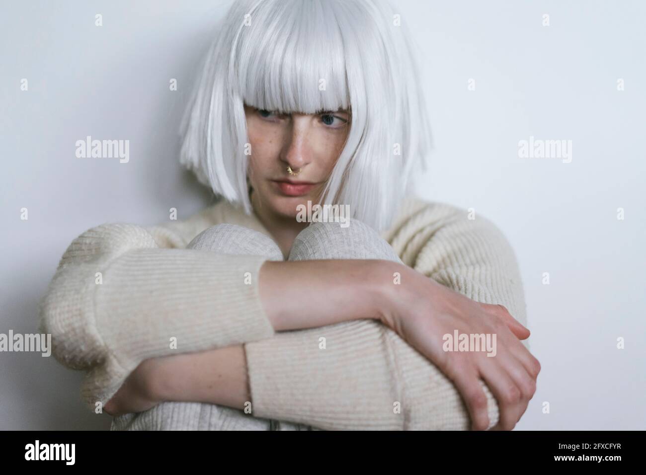 Woman hugging knees in front of wall Stock Photo - Alamy