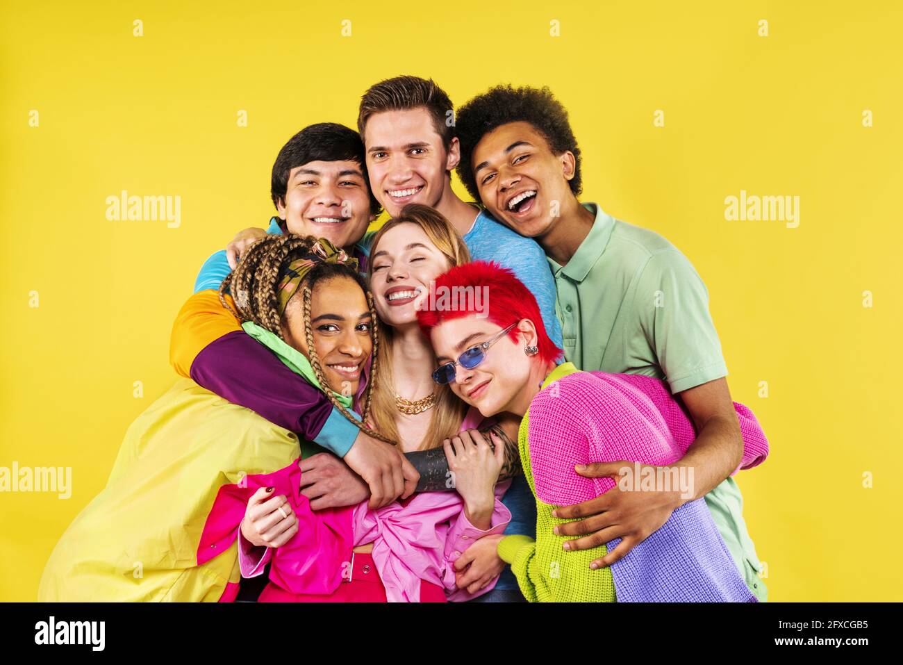Young friends embracing each other while standing in front of yellow ...