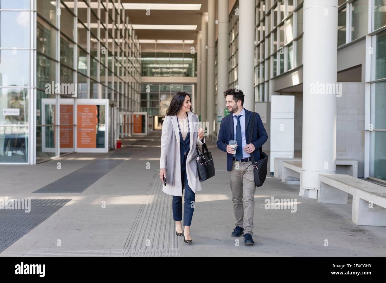 Male and female colleagues talking while walking on footpath Stock ...