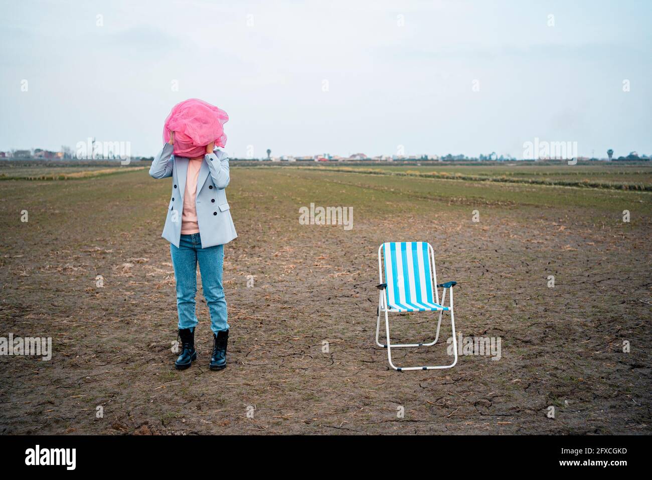 Young woman covering face with tulle net by chair on drought ...