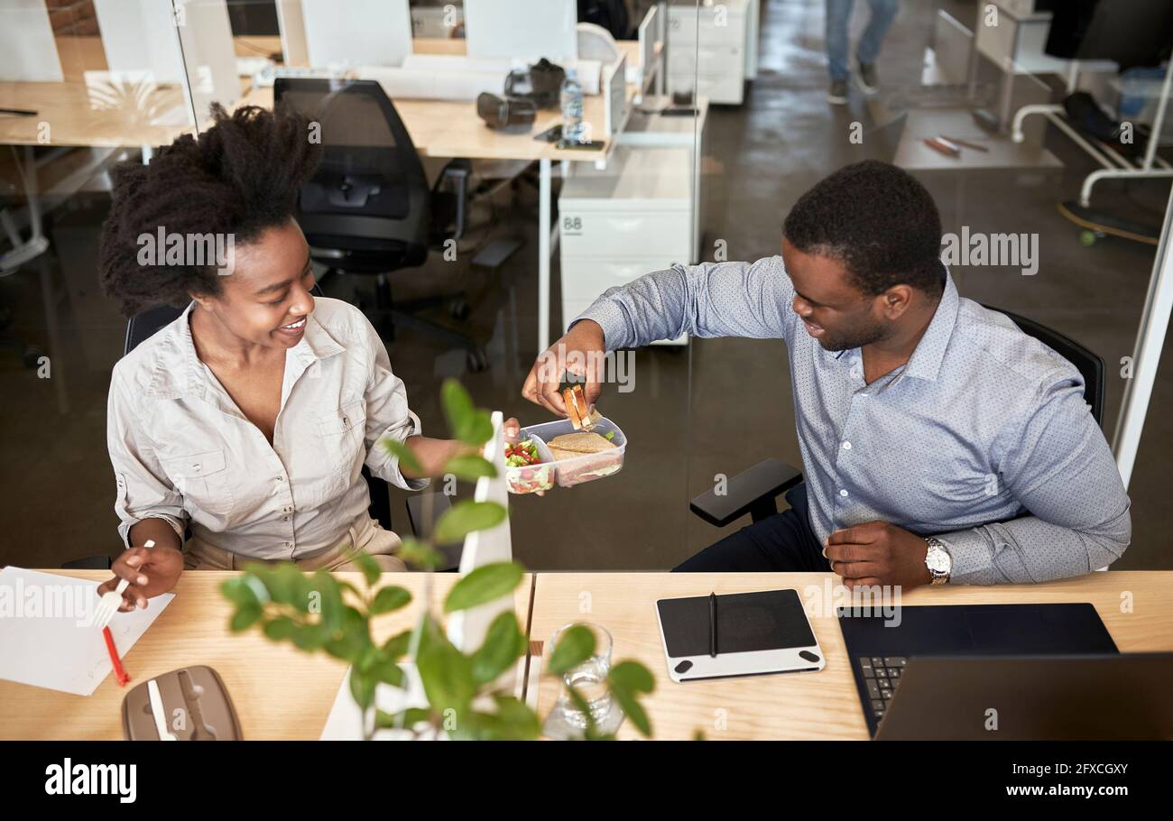 Male And Female Coworkers Sharing Sandwiches During Lunch Break At