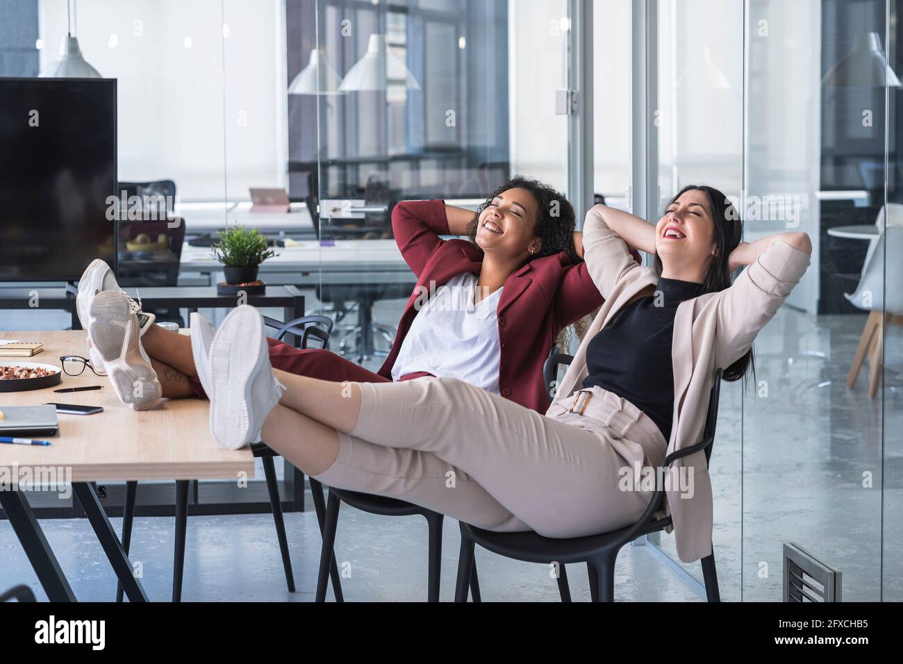 Smiling female professionals with eyes closed relaxing on chair in ...