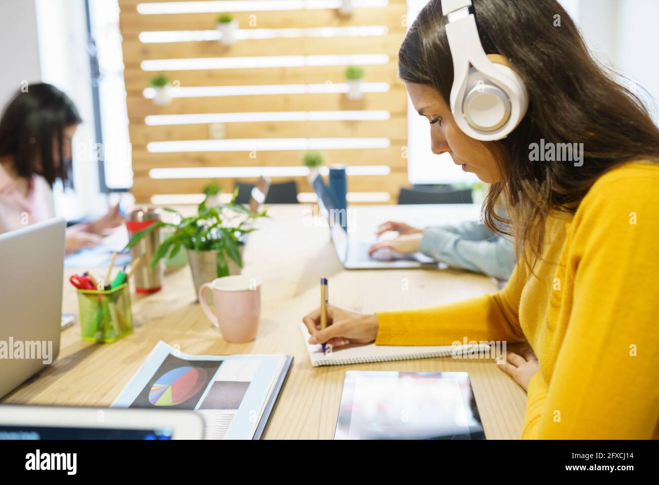 Female professional wearing headphones writing while working in office ...