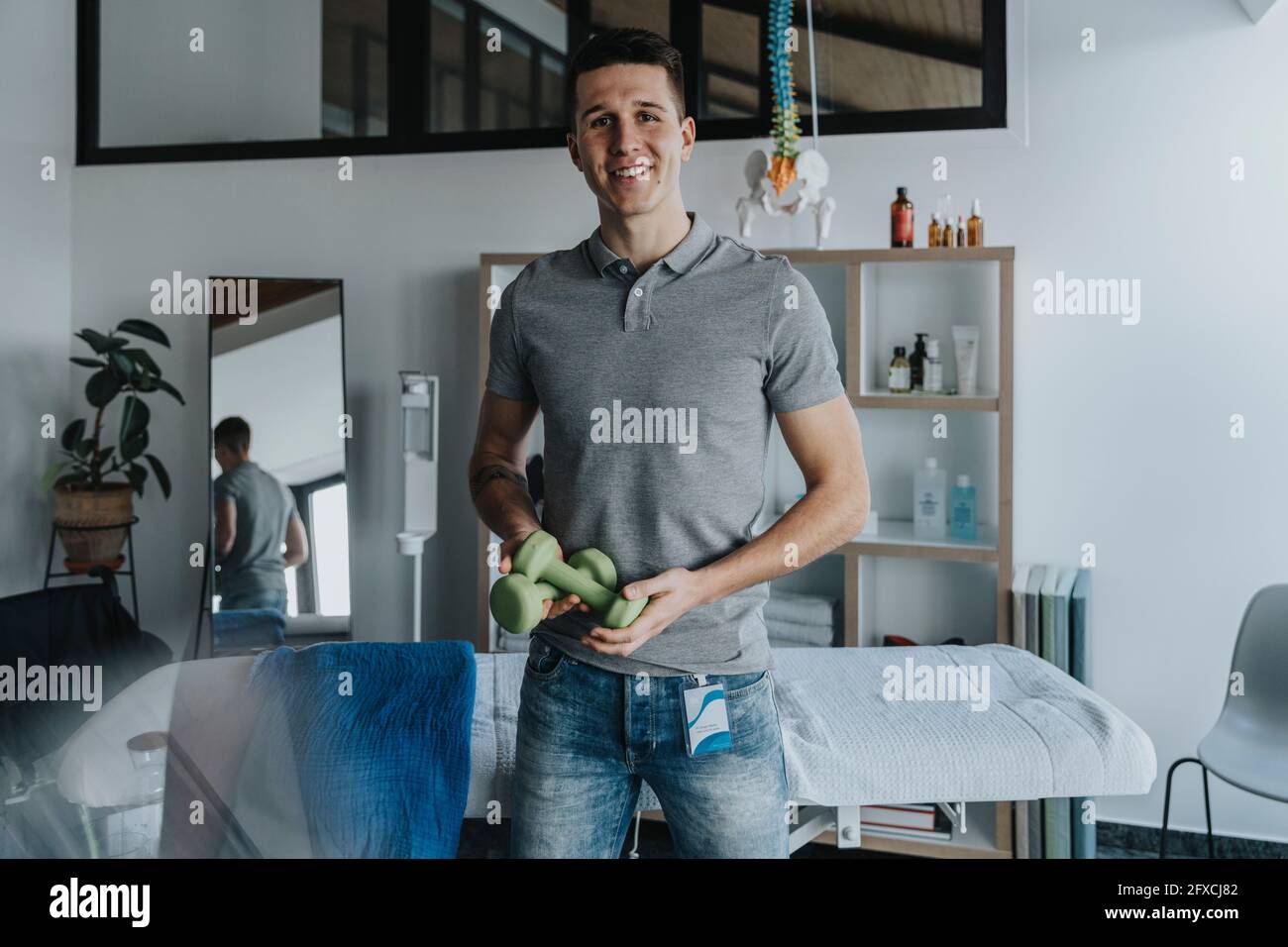 Smiling male physiotherapist with weights standing in practice Stock ...