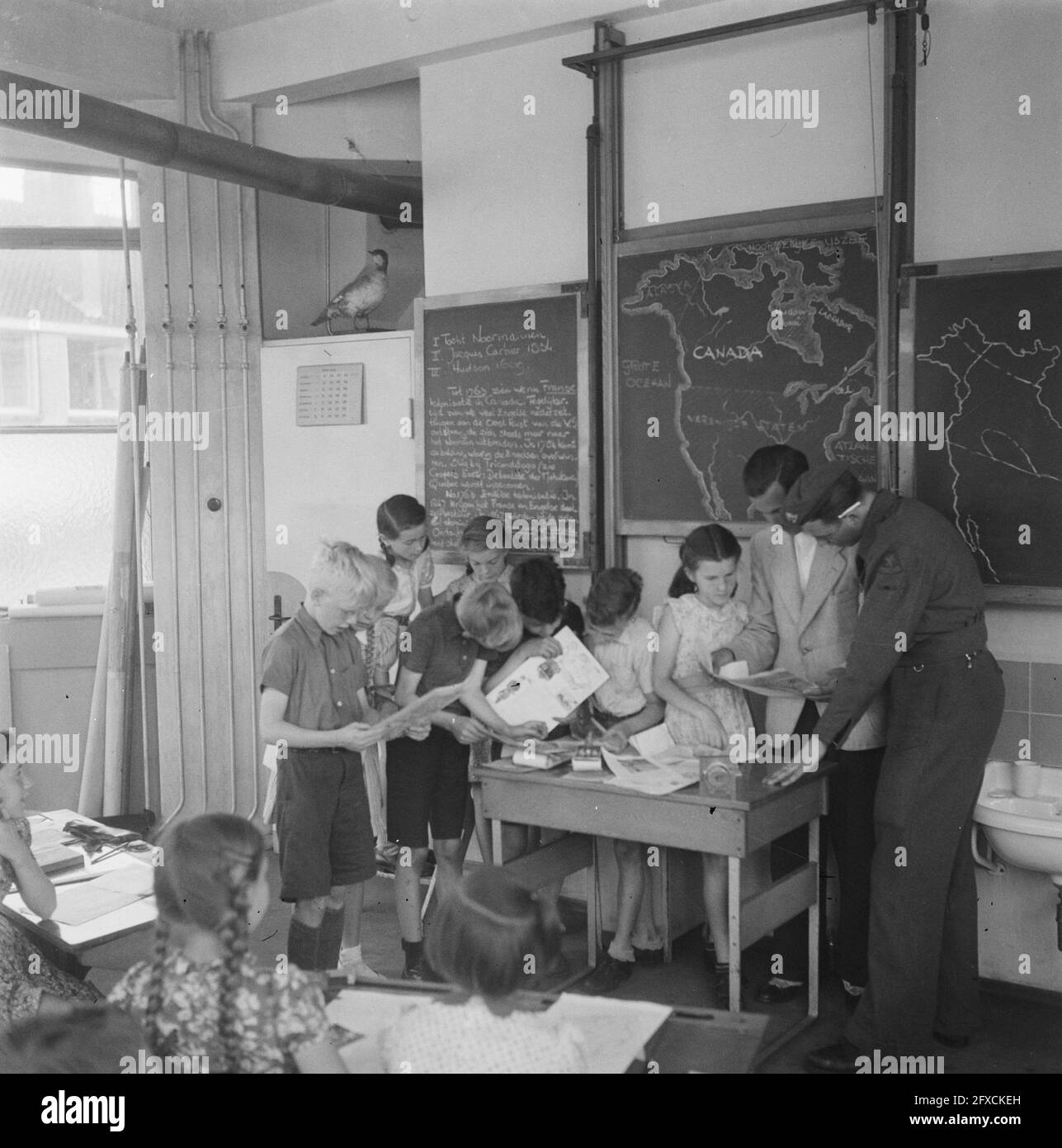 [Children crowd around the teacher's table, beside the teacher a man in ...