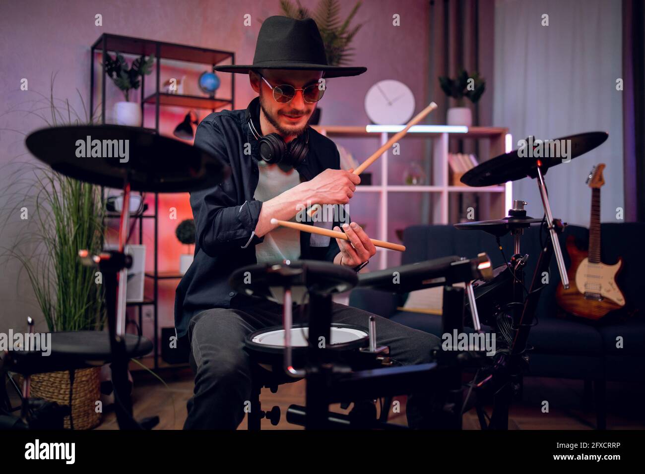 Happy stylish man sitting at dark music studio and playing electronic ...