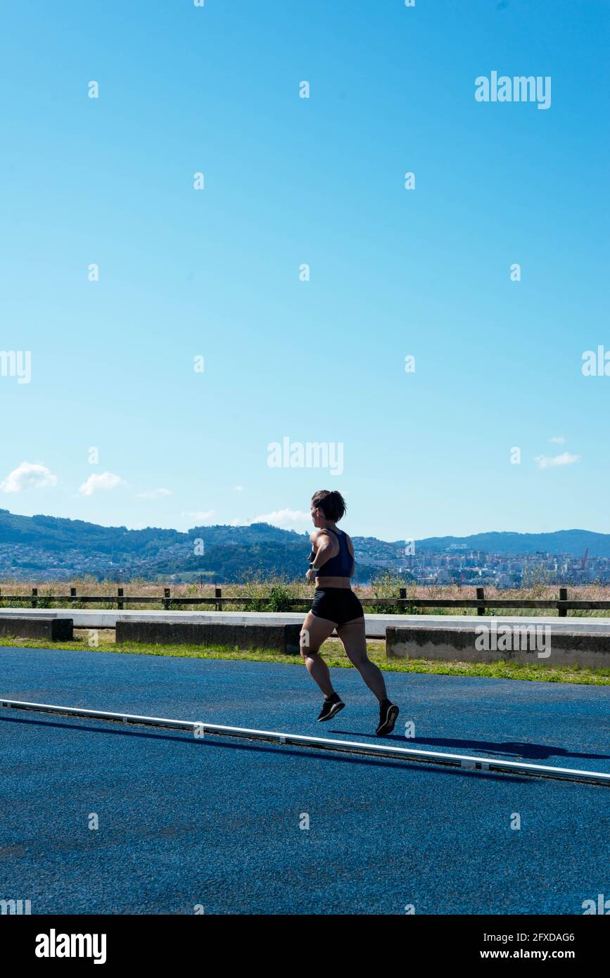 Back view of a young female sprinter running on an athletics track ...