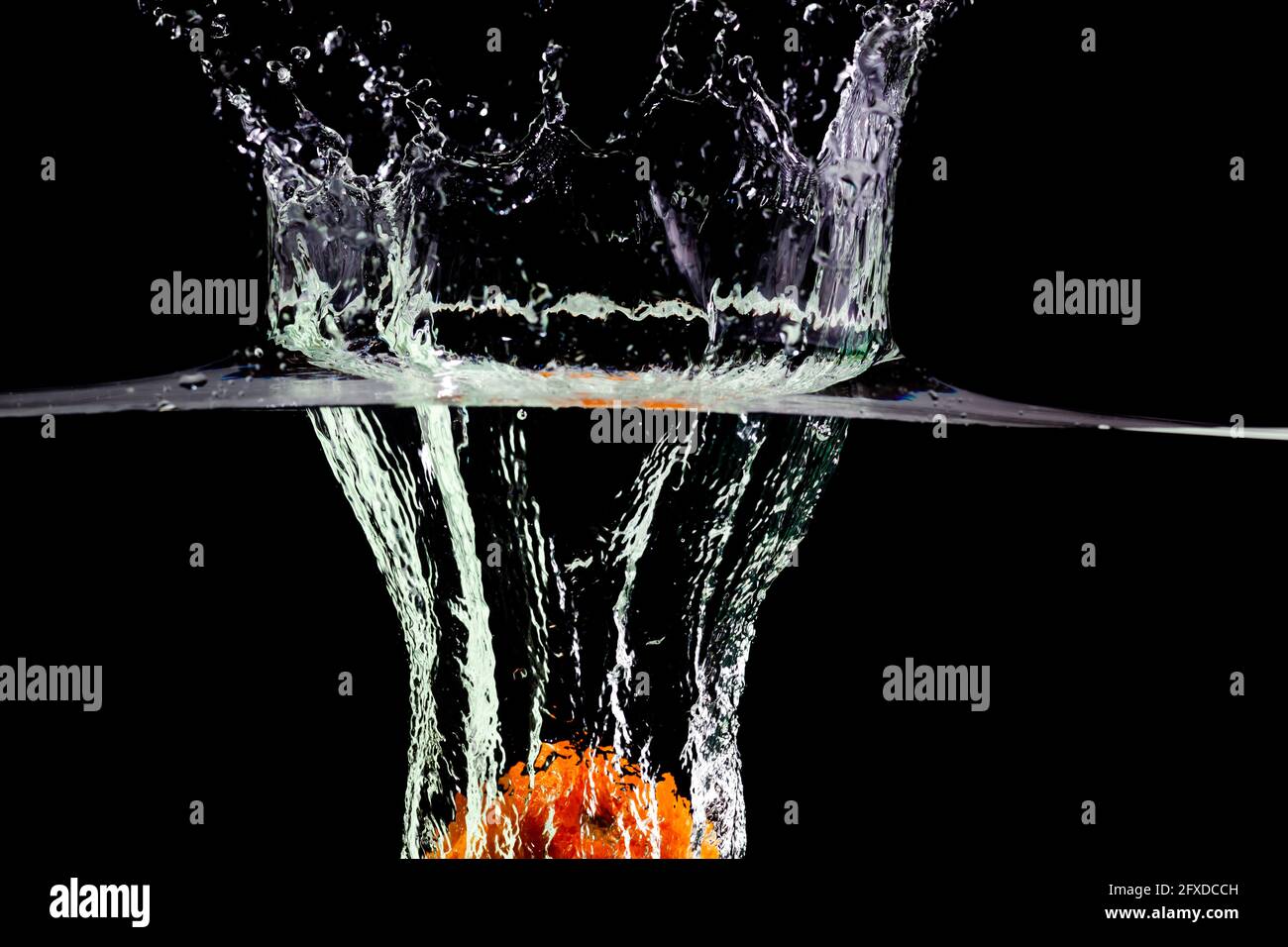 fruit orange falls into the water with splashes on a black background ...