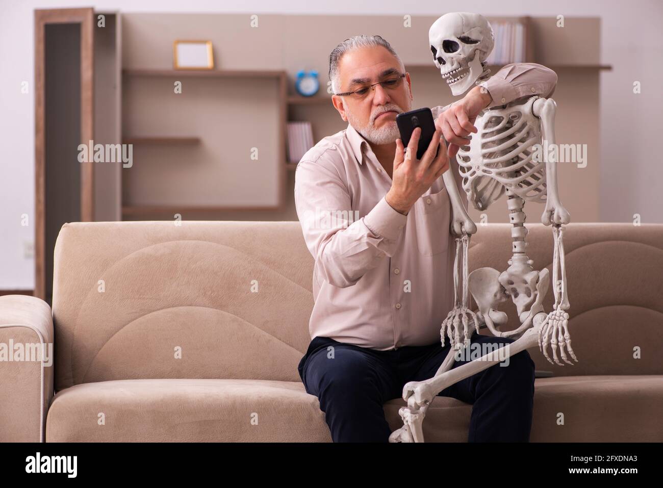 Old man sitting on the sofa with the female skeleton in undying love ...