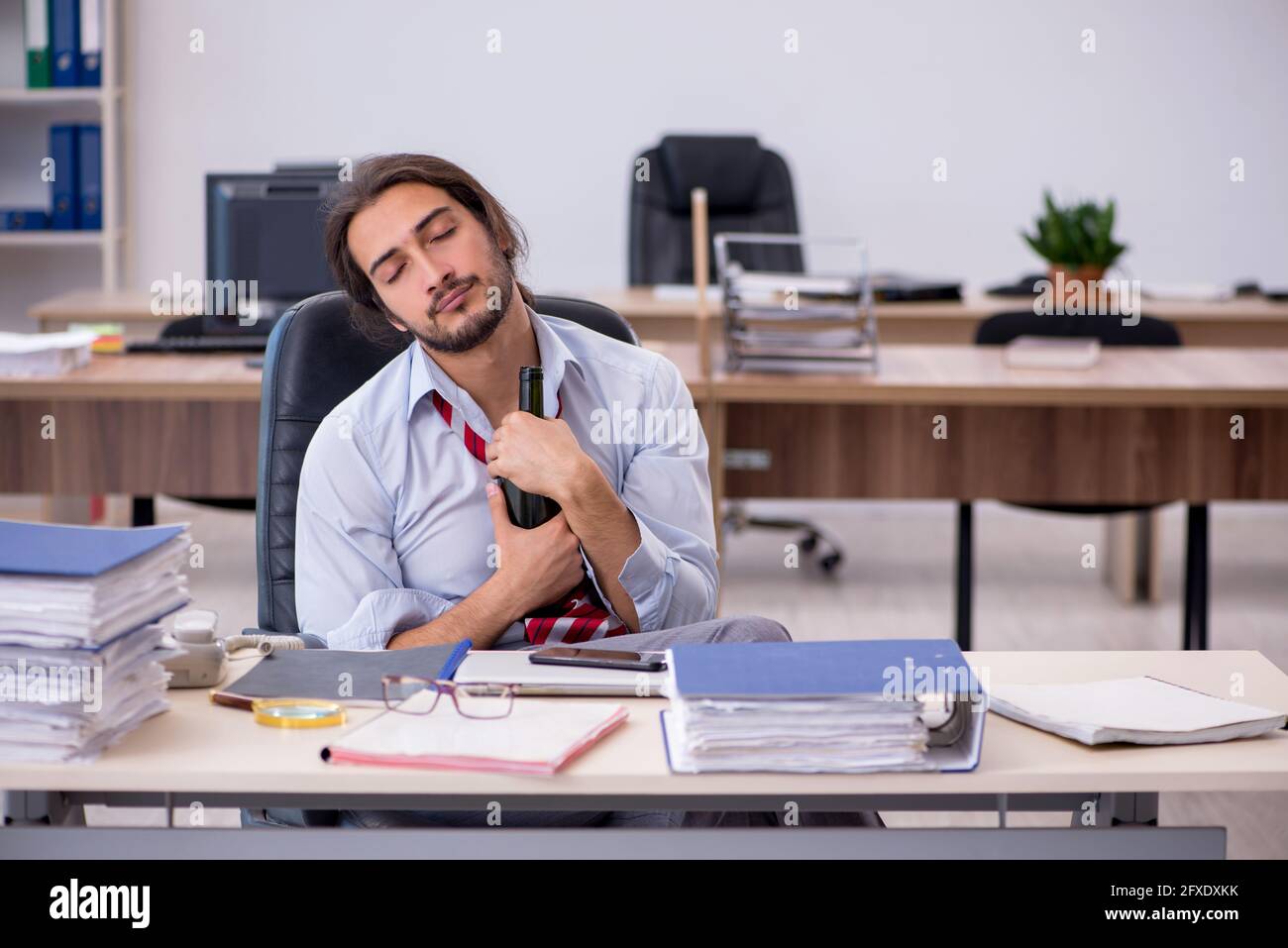 Young male employee drinking alcohol at workplace Stock Photo - Alamy