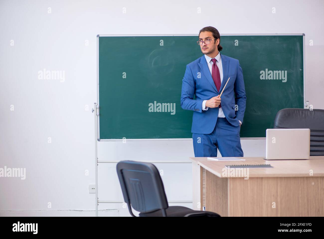 Young teacher in suit in front of green board Stock Photo - Alamy