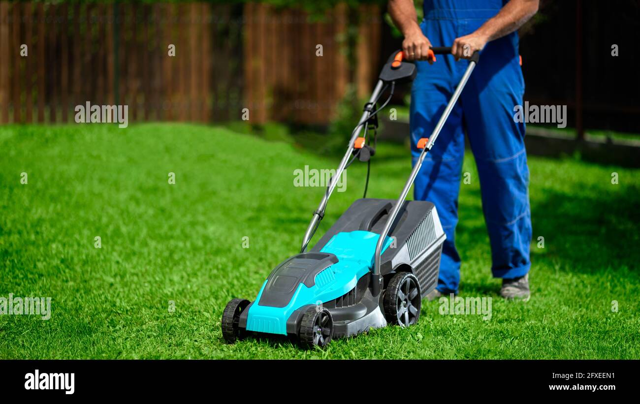 Male worker on the street working on mowing the lawn with the help of a ...