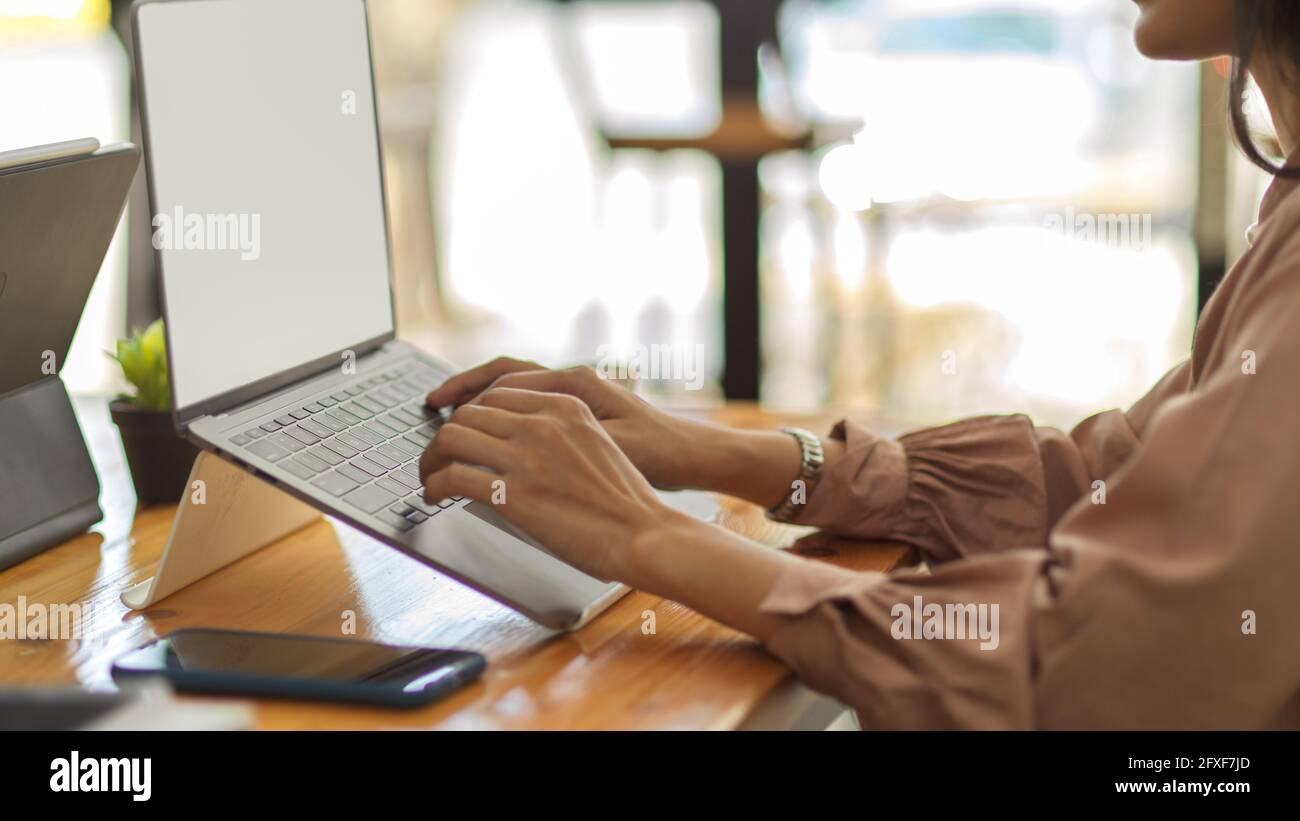 Side view of female hands typing on laptop keyboard on wooden desk in ...