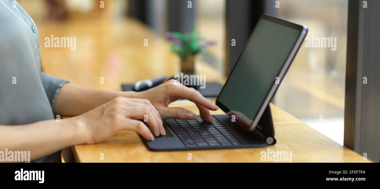 Close up view of female hands typing on tablet keyboard on wooden bar ...