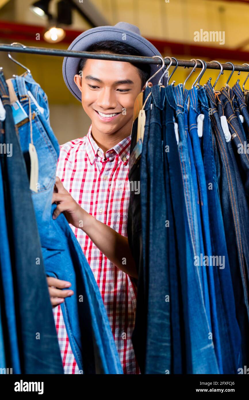Asian man browsing jeans hanging on a clothes rack in fashion store ...