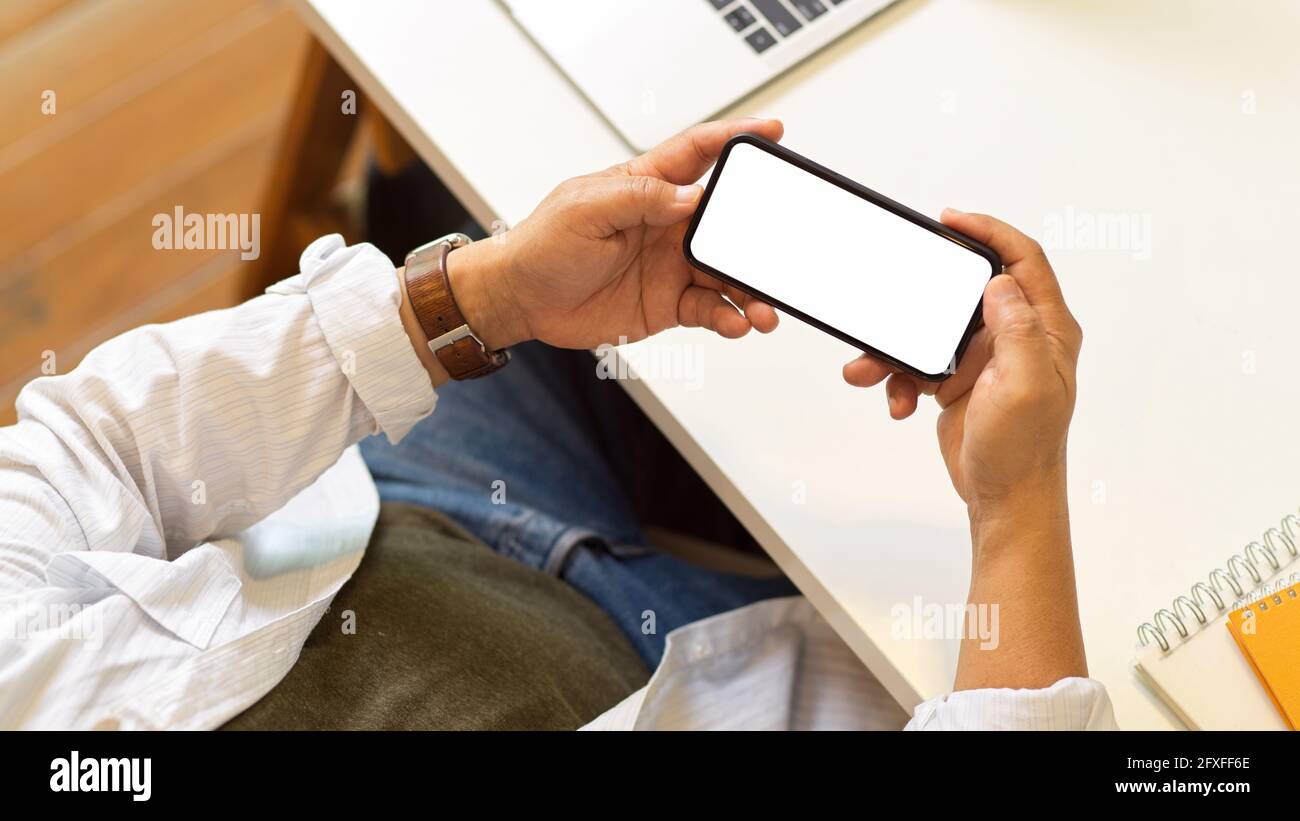 Top view of male freelancer hands holding horizontal smartphone with mock up screen above ...