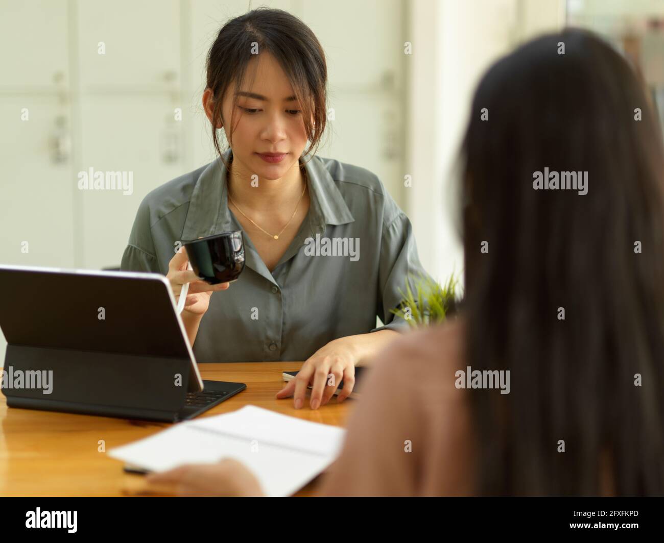 Portrait of two female office worker consulting other work while ...