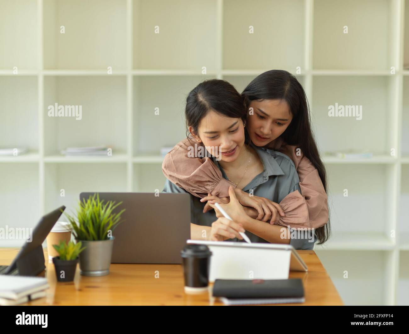 Portrait of two female office workers hugging in office room, happy ...