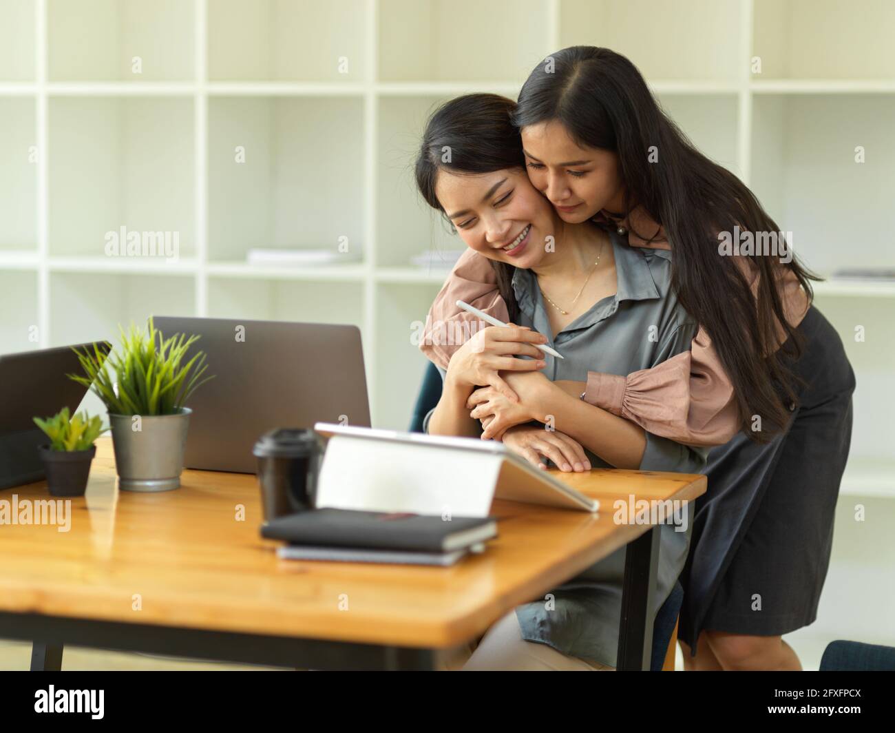 Portraits of two female office workers hugging while working in office ...
