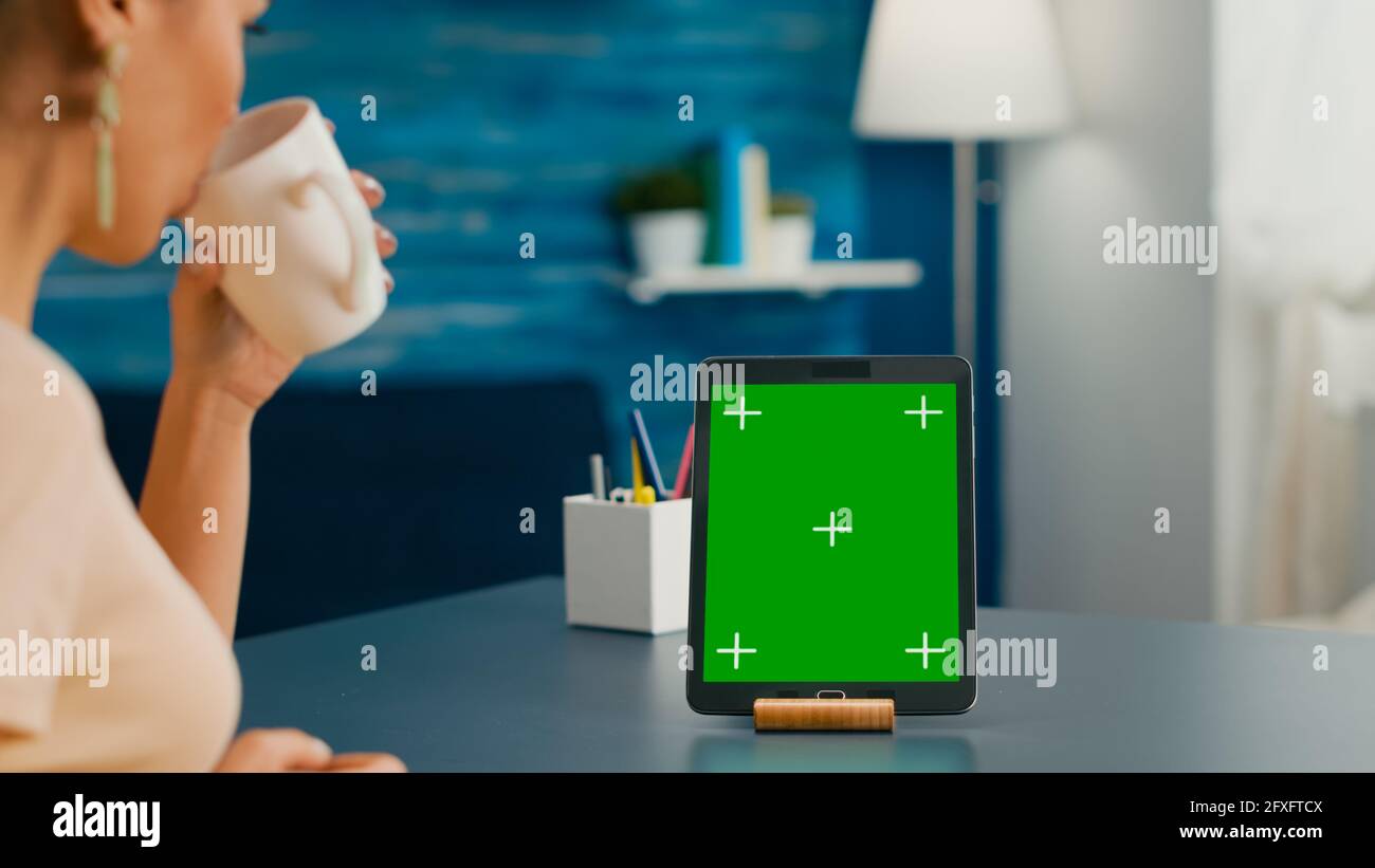 Woman drinking a cup of coffee while looking at tablet computer with ...