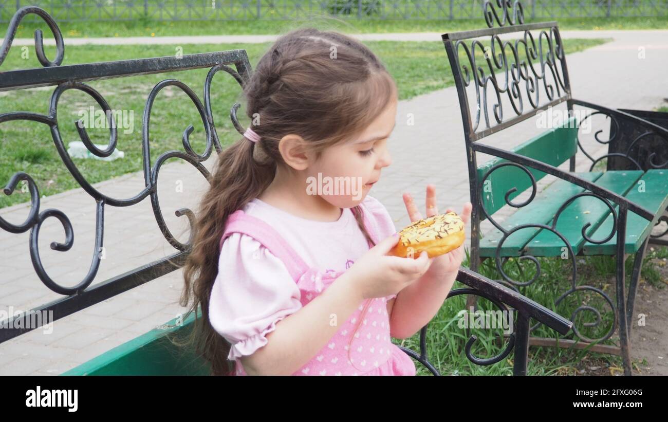 girl on a park bench eating a donut with yellow frosting. happy ...
