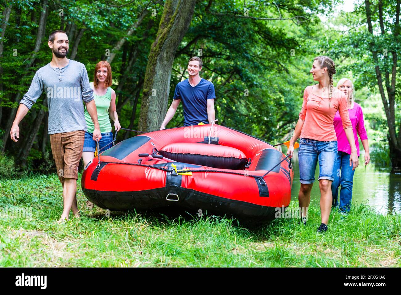 Friends carrying rubber boat to forest river Stock Photo - Alamy