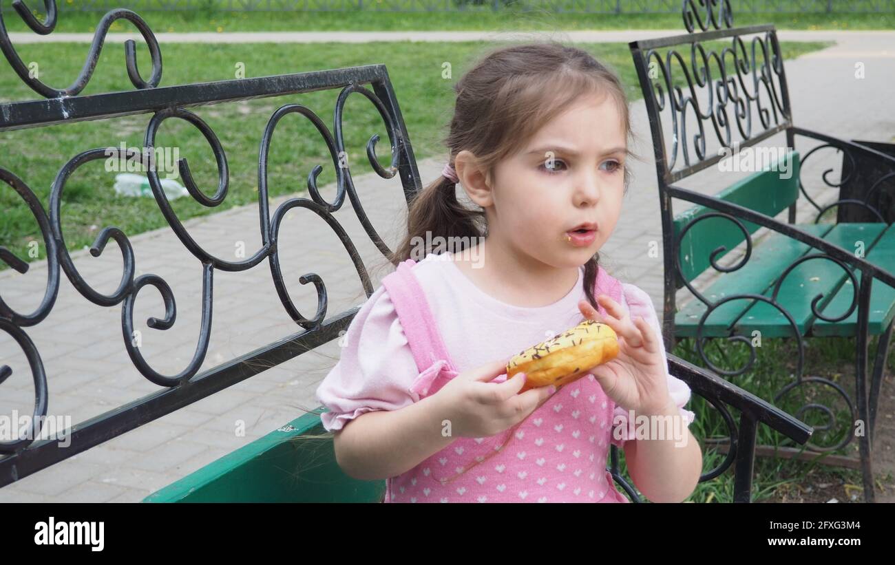 girl on a park bench eating a donut with yellow frosting. happy ...