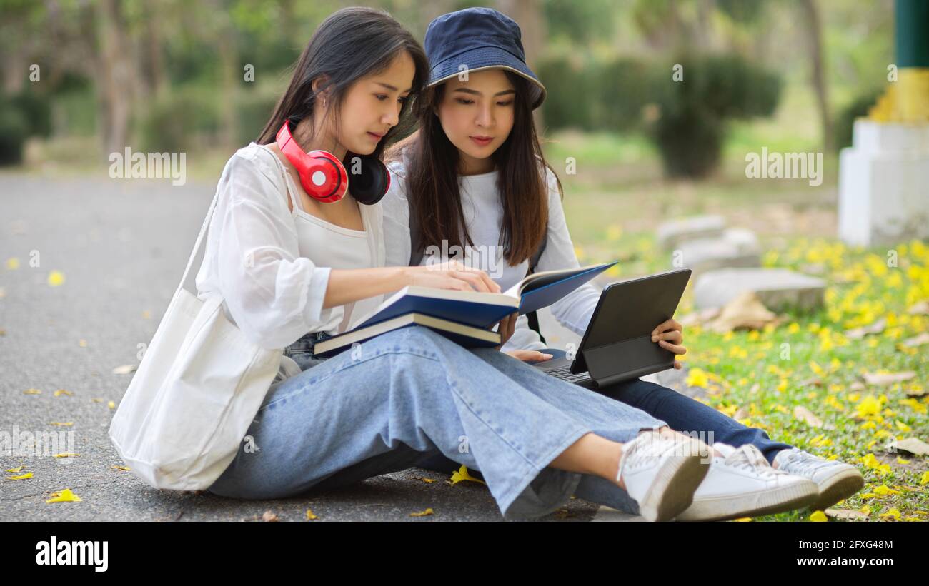 Side view of female students outdoor studying together, reading books ...