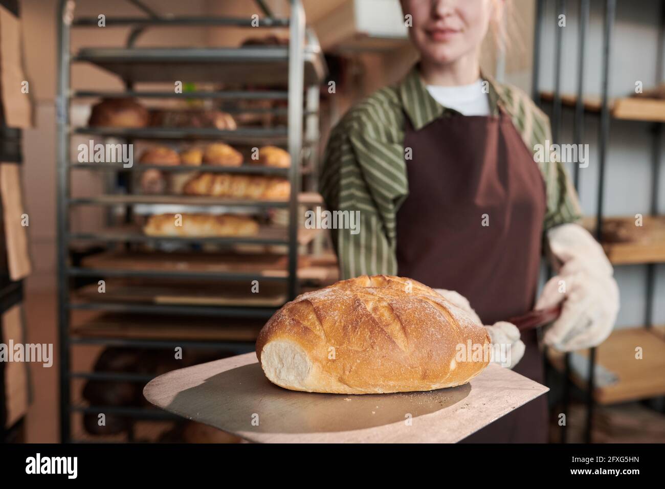 Young baker in uniform taking the bread out of the oven Stock Photo - Alamy