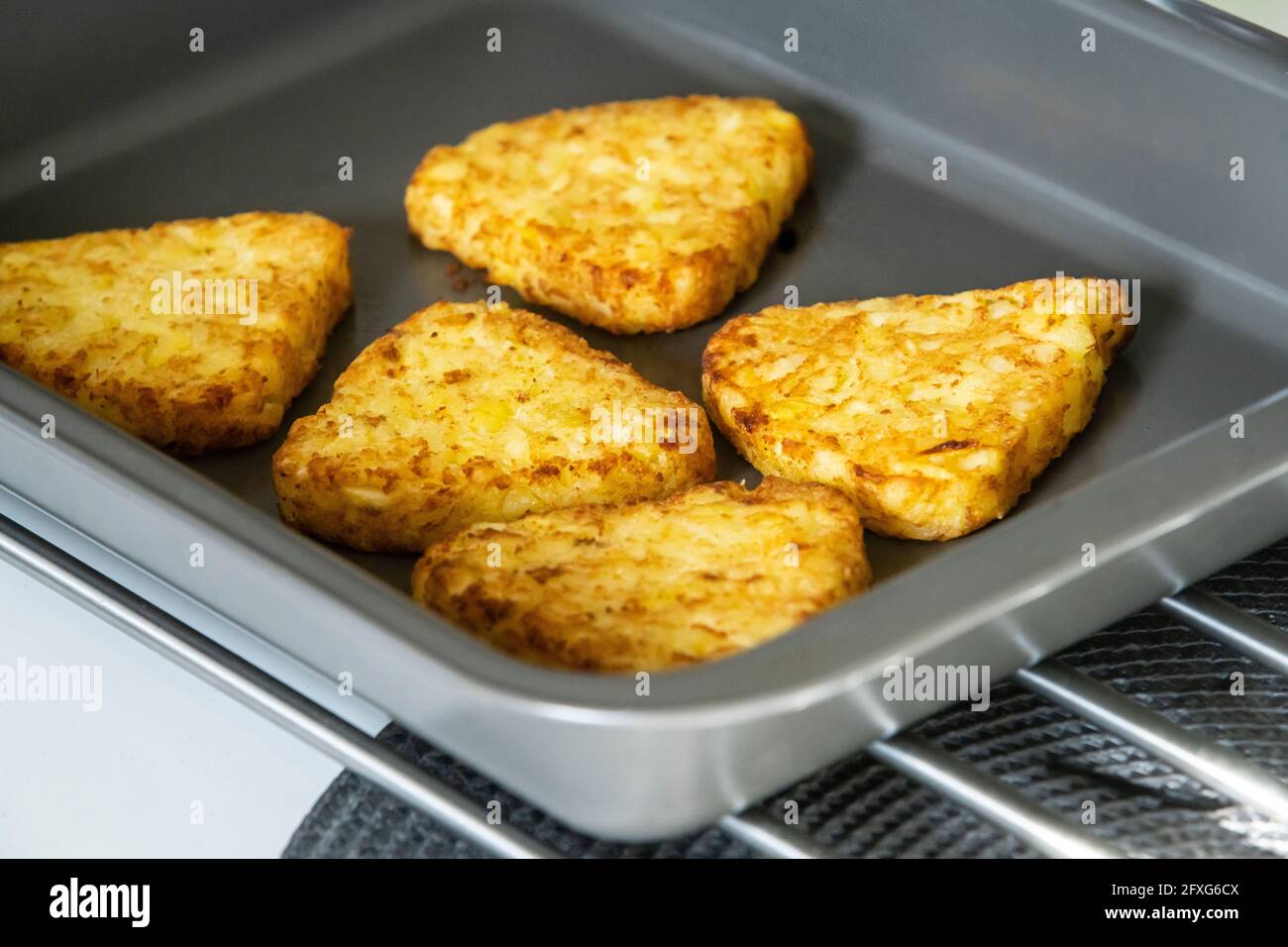 A non-stick tray of 5 triangular potato hash browns freshly baked out ...