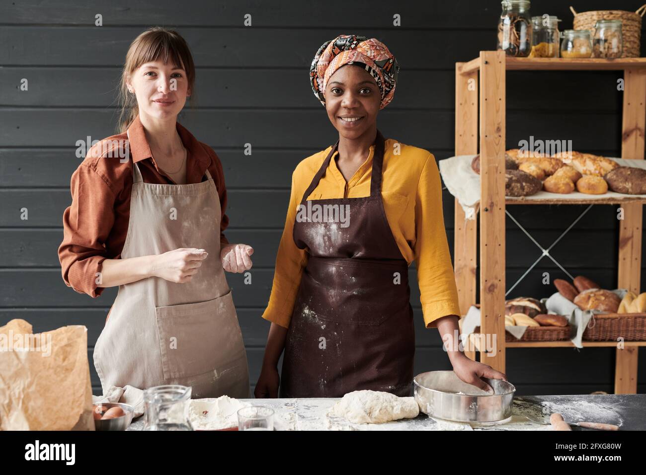 Portrait of two young bakers smiling at camera while standing in the ...