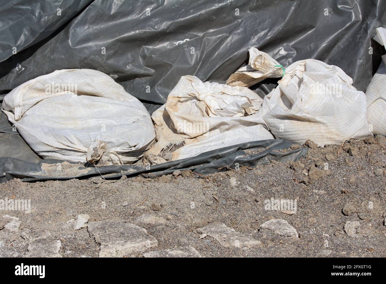 Row of new and old broken white sandbags holding thick dark nylon ...