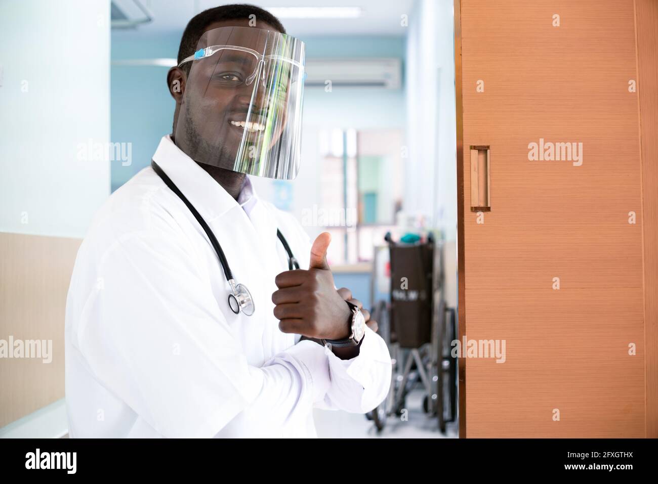 Portrait of african male doctor in face shield standing in lab coat ...