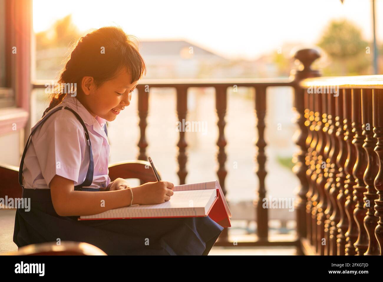Cute uniform little girl student is writing a book and smiling with ...