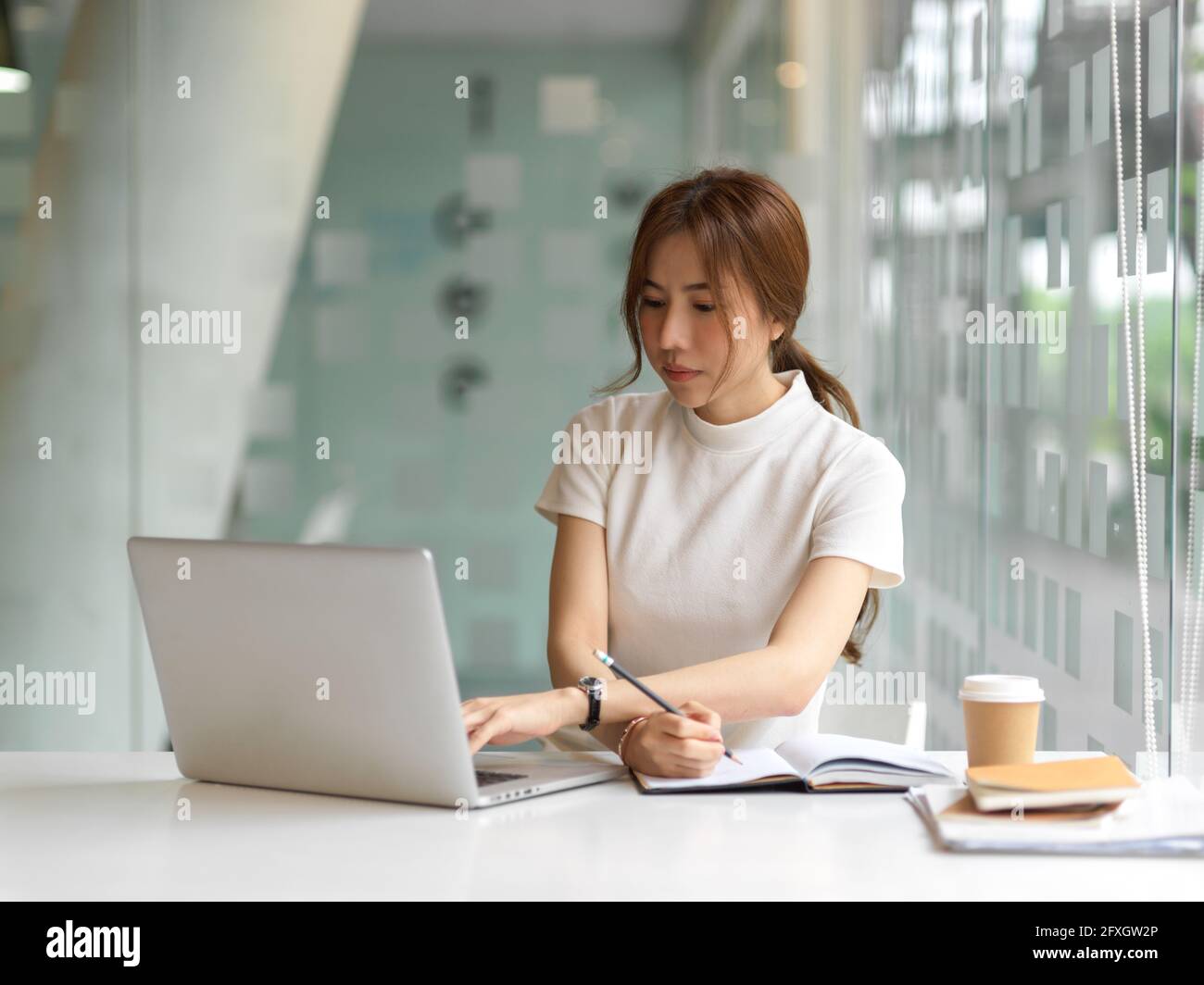 Portrait of female student doing assignment with laptop and paperwork ...