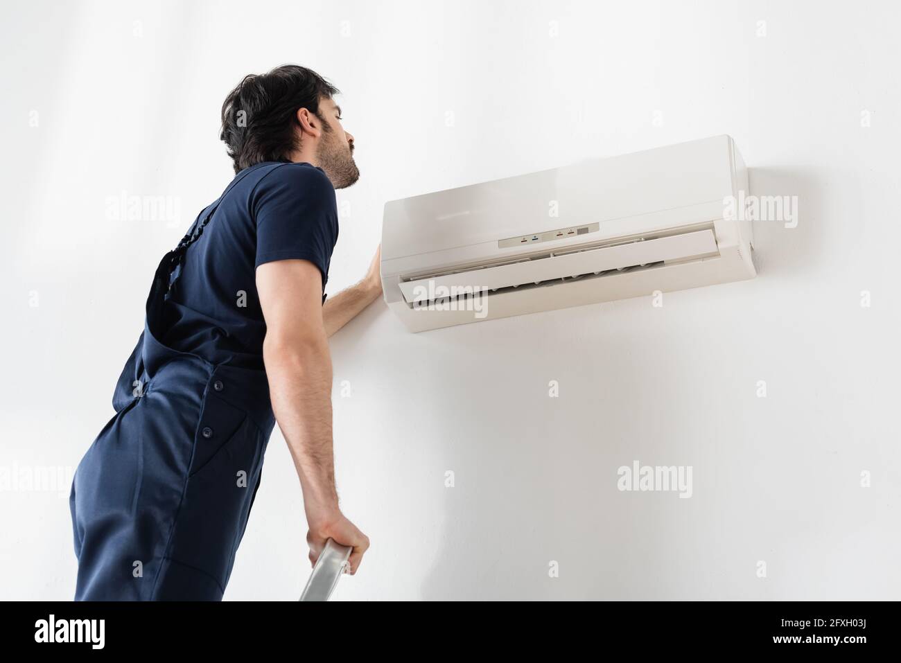 handyman in overalls standing on ladder while fixing broken air ...