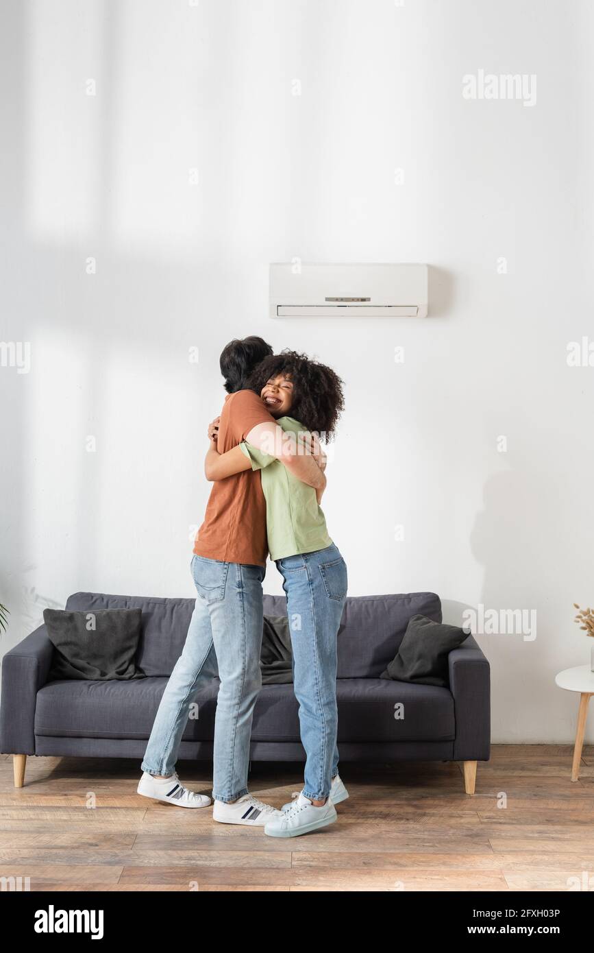 happy multiethnic hugging near fixed air conditioner in modern living ...