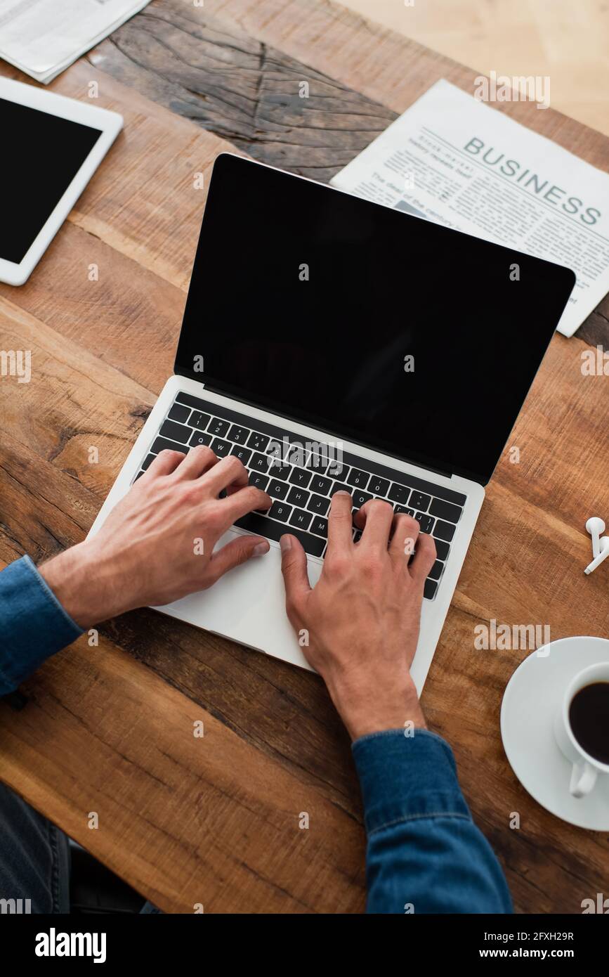 partial view of freelancer typing on laptop near newspaper and cup of ...