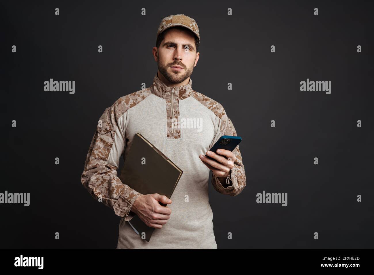 Serious military man using cellphone while posing with folder isolated ...