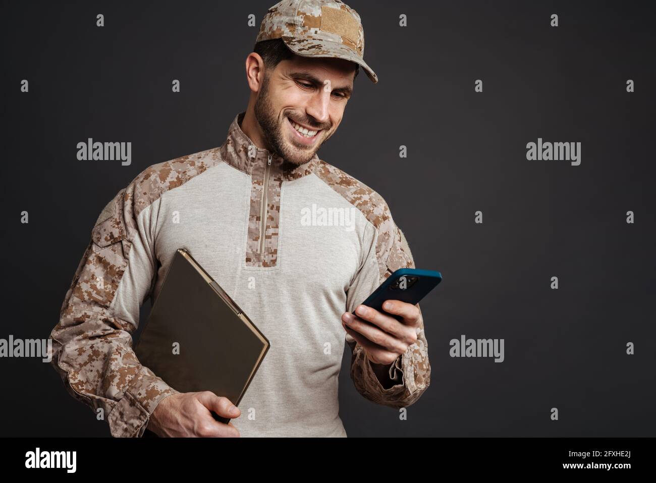 Serious military man using cellphone while posing with folder isolated ...