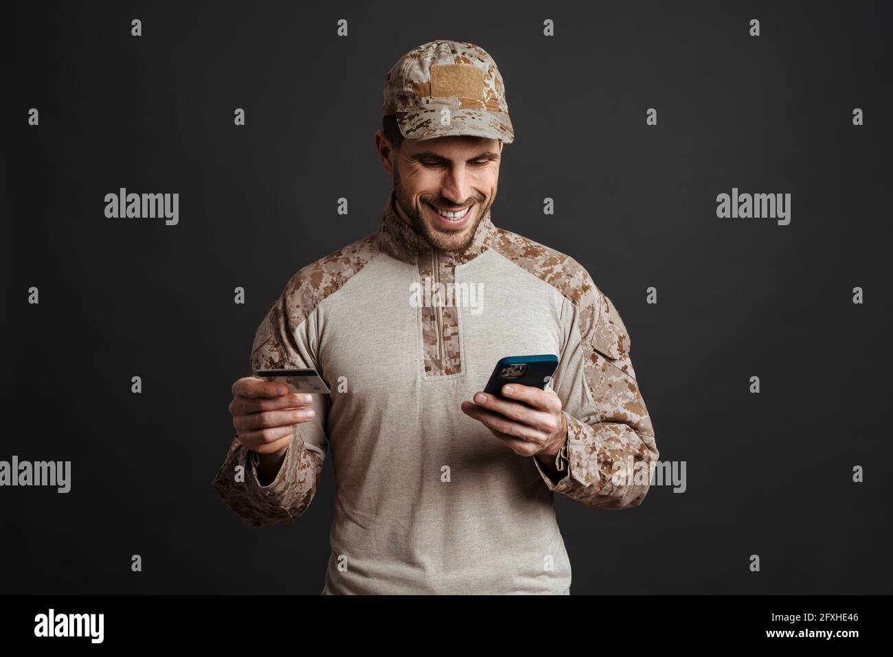 Excited military man posing with cellphone and credit card isolated ...