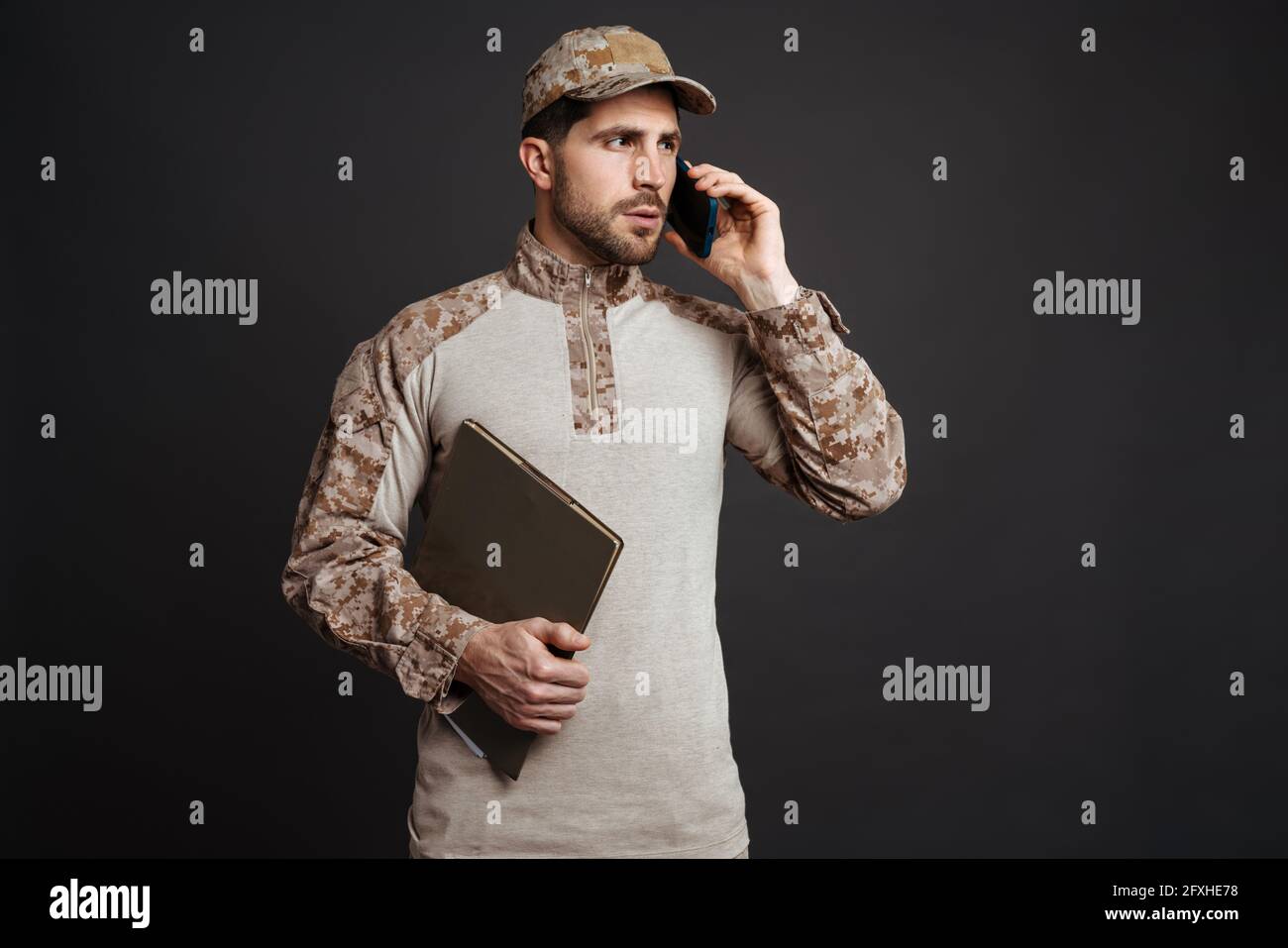 Serious military man talking on cellphone while posing with folder ...